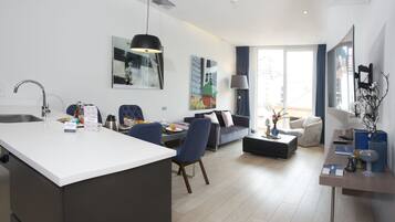Quarto de hotel moderno com cozinha, espaço para refeições e área de estar com sofá e poltronas.