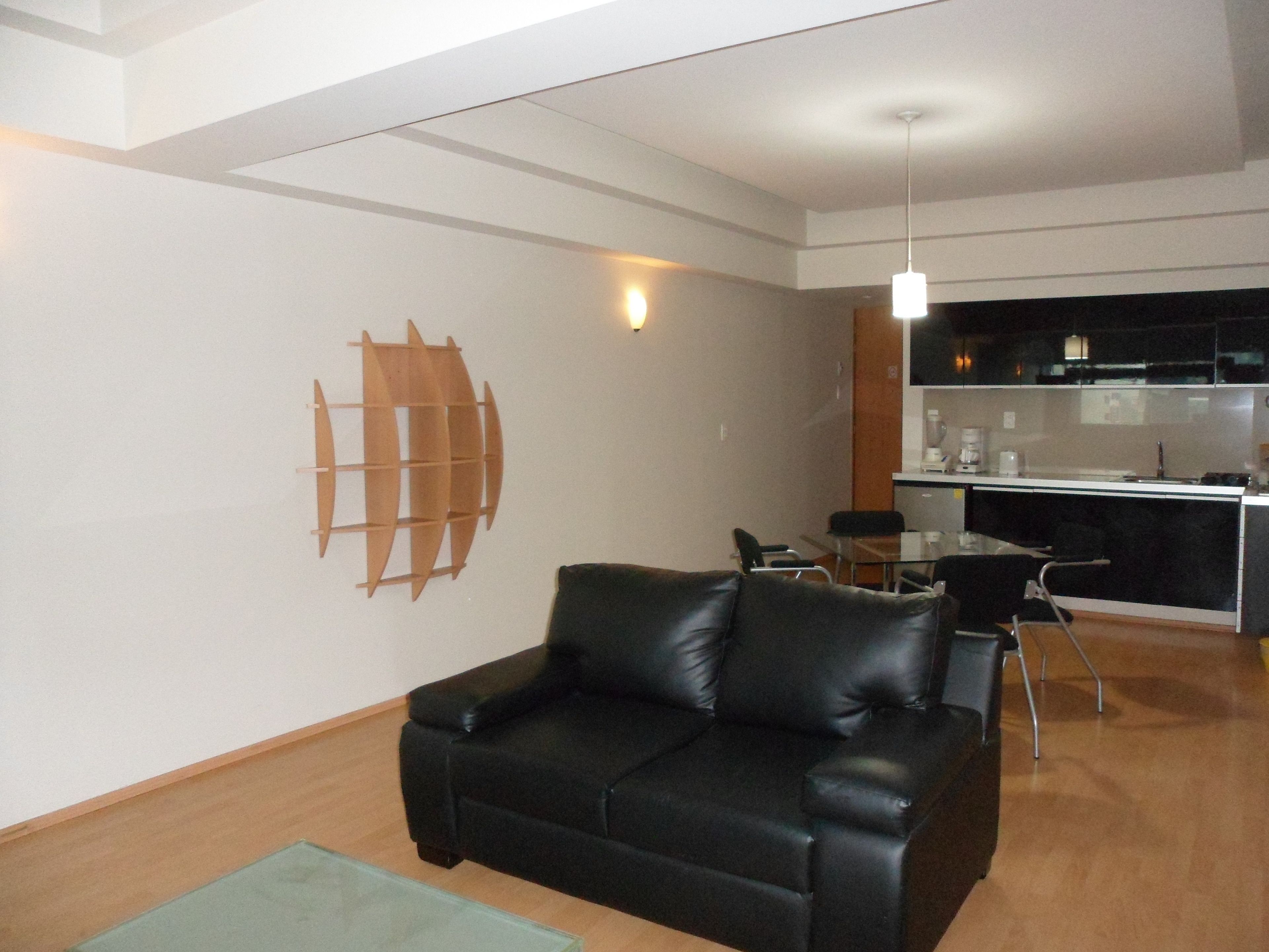 Uma sala de estar moderna com um sofá de couro preto, uma área de jantar e uma cozinha ao fundo.