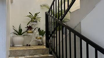 Uma escadaria com corrimão preto, que leva a um patamar com luminária na parede.