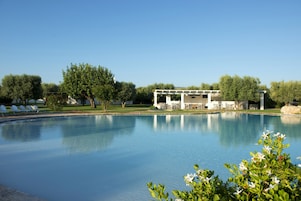 Piscina com espreguiçadeiras e um edifício com área de estar externa.