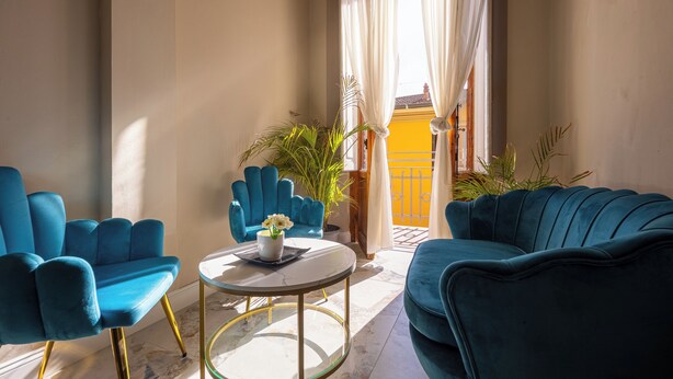 Quarto com um sofá azul, uma poltrona combinando e uma mesinha de centro com um vaso de flores.