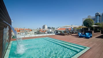 Piscina no terraço com um recurso aquático, cadeiras de descanso e vista para a paisagem urbana.