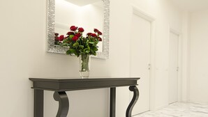 Um corredor com piso de mármore, uma mesa consola com um vaso de rosas vermelhas e um espelho com moldura em padrão de zebra.