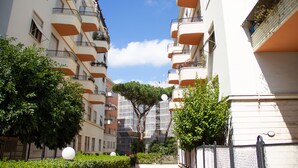 Uma rua urbana estreita, com edifícios altos, varandas e muita vegetação.