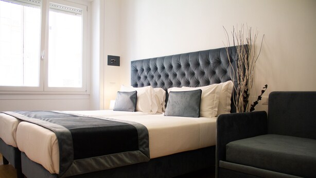 Quarto moderno com cama grande, cabeceira estofada escura e sofá escuro.
