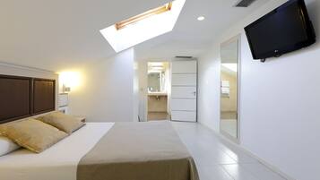 Quarto de hotel com cama, televisão, claraboia, banheiro e espelho.