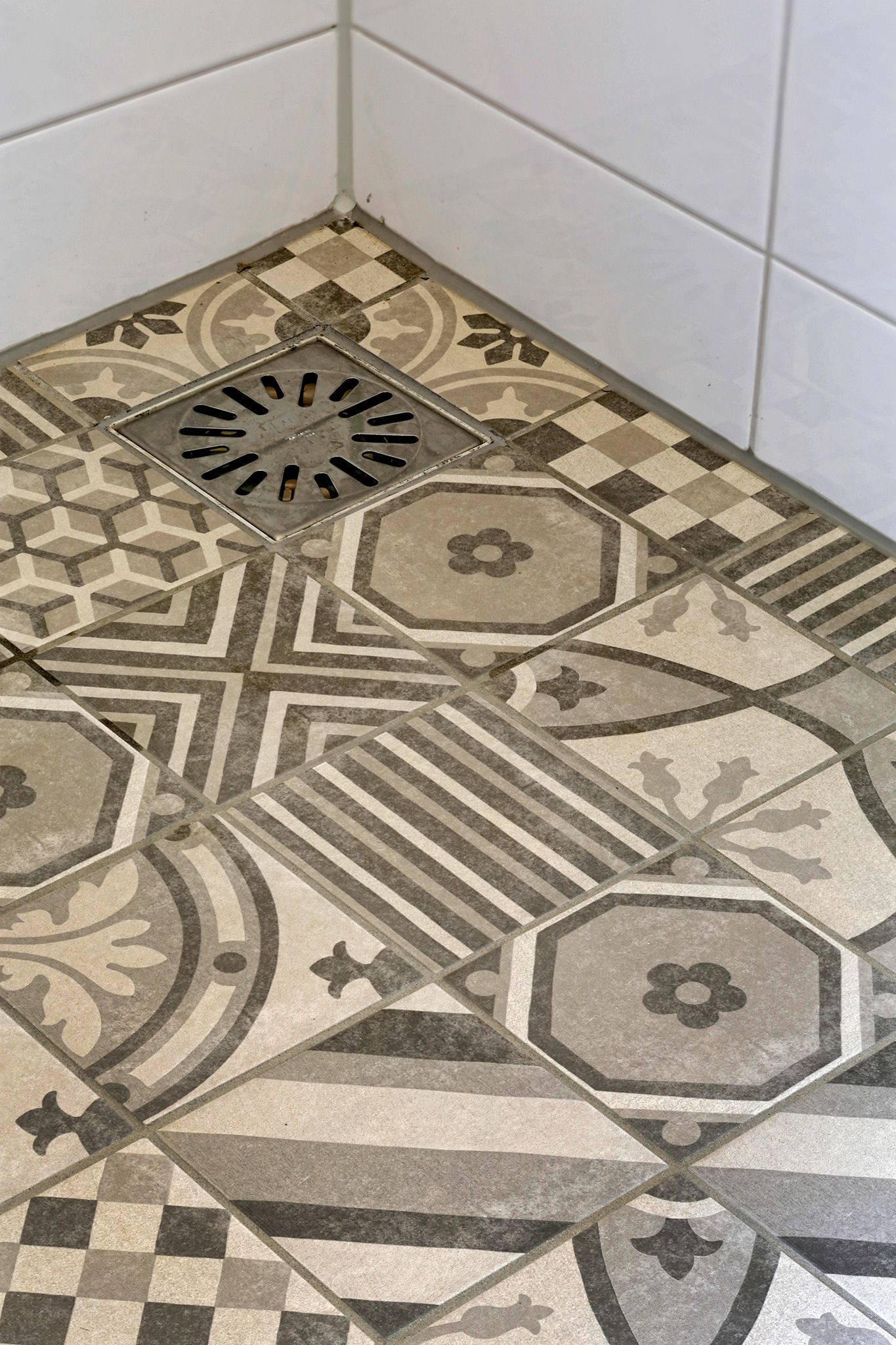 Um canto de banheiro com piso de azulejos estampados e um ralo.