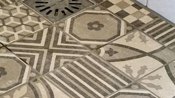 Um canto de banheiro com piso de azulejos estampados e um ralo.