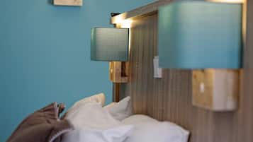 Uma cama bem arrumada com roupa de cama branca e castanha, uma cabeceira de madeira e uma luminária fixada na parede.