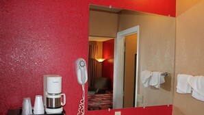 Casa de banho de hotel com uma parede vermelha, uma pia, um espelho, um secador de cabelo, uma máquina de café e um micro-ondas.
