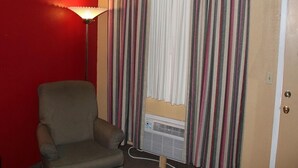 Quarto com uma poltrona, janela com cortinas listradas, luminária de pé e ar-condicionado fixado na parede.