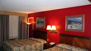 Quarto de hotel com duas camas, mesa de cabeceira com abajur e duas fotos emolduradas na parede.