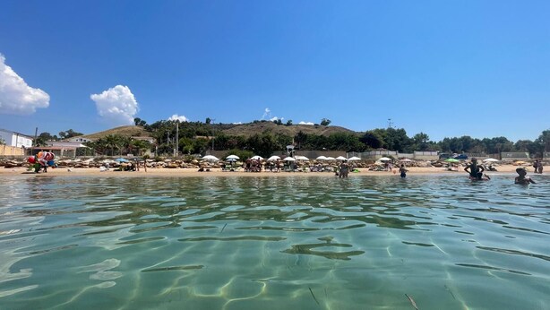 Uma praia com água cristalina, guarda-sóis e pessoas.