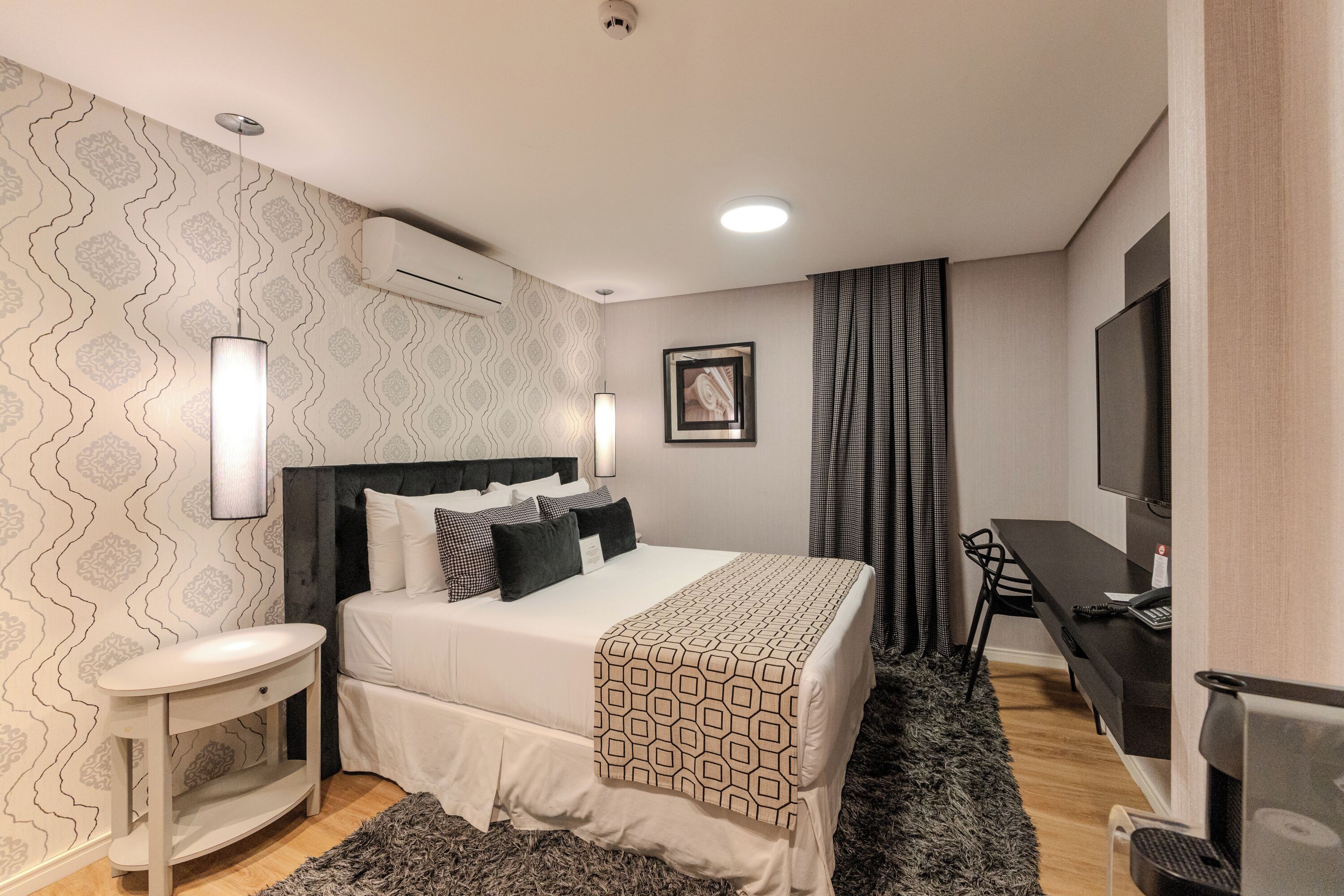 Quarto de hotel moderno com uma cama grande, mesa de cabeceira e escrivaninha com cadeira.