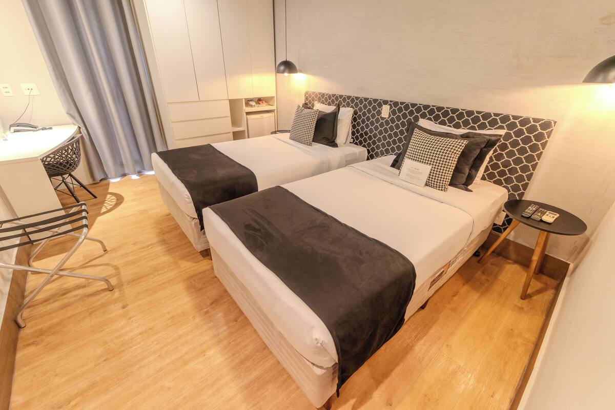 Quarto de hotel com duas camas, uma escrivaninha e uma cadeira.