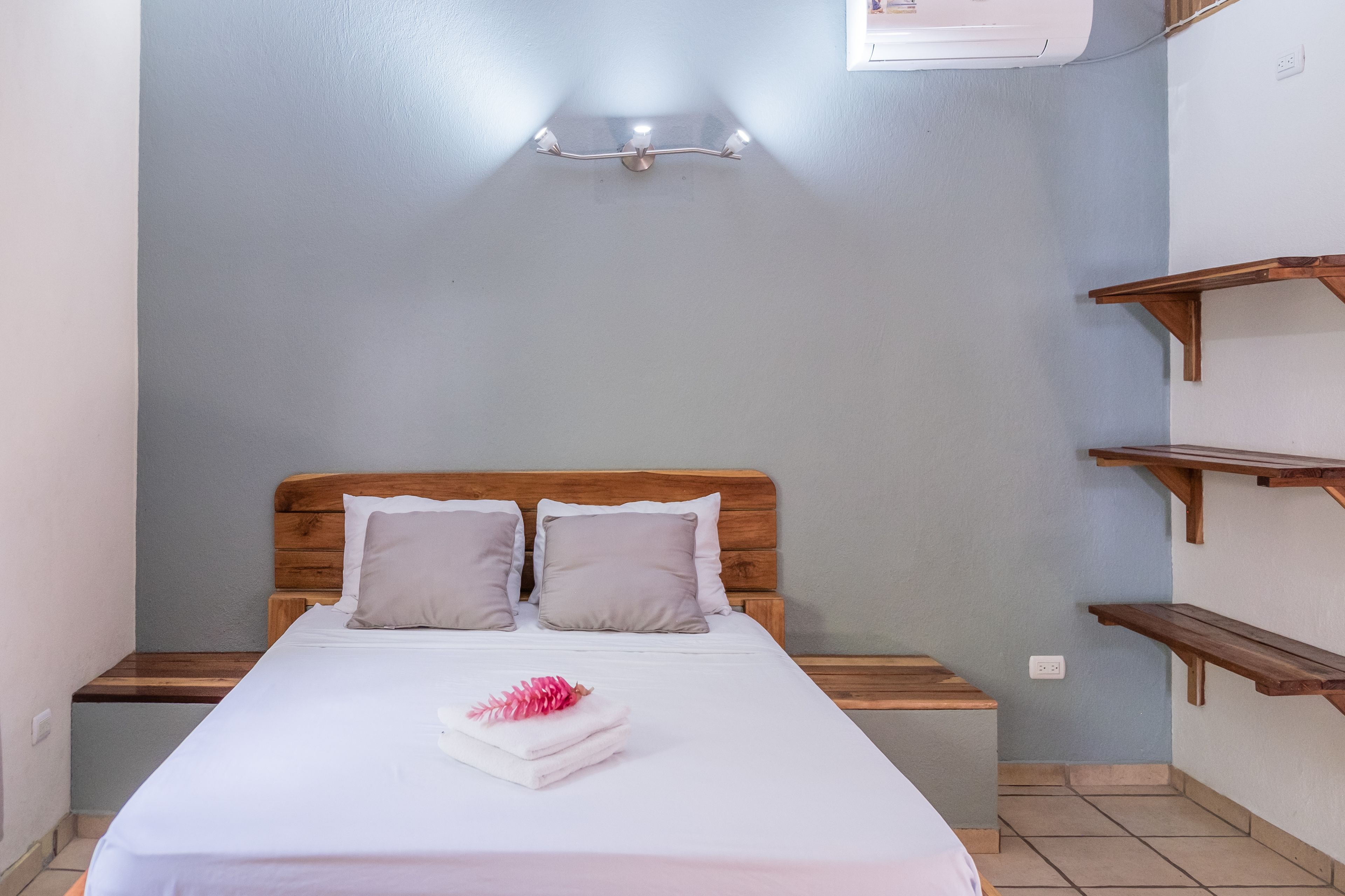 Uma cama bem arrumada com cabeceira de madeira, mesa de cabeceira e prateleira na parede.