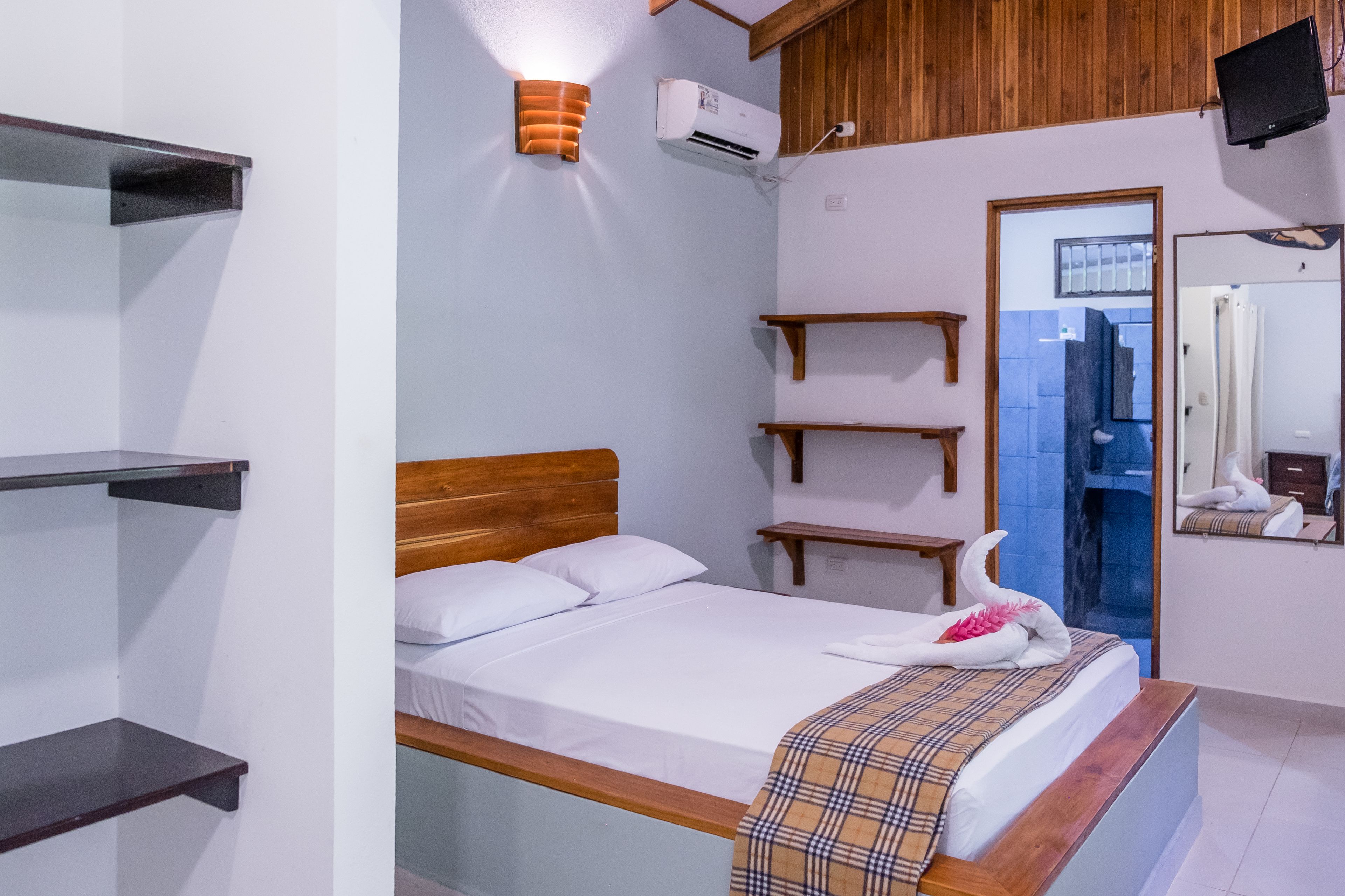 Quarto com cama de madeira, roupa de cama branca, ar condicionado fixado na parede e espelho com toalha.