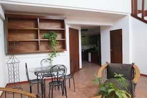 Uma área de refeições com uma mesa, cadeiras, uma prateleira de madeira e um vaso com planta.