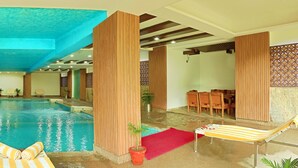 Piscina com tapete vermelho, pilares de madeira e cadeiras de descanso.