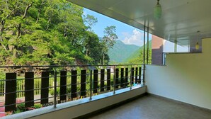 Uma varanda com grade de metal, vista para uma paisagem verdejante com árvores e montanhas.