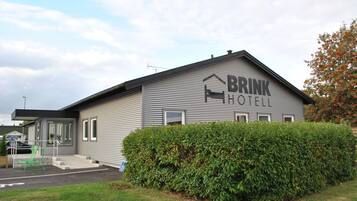 BRINK HOTEL com design moderno, apresentando uma entrada ampla e um conjunto de arbustos bem cuidados.