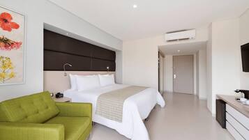 Quarto de hotel moderno com uma cama grande, um sofá verde, uma televisão de tela plana e um quadro na parede.
