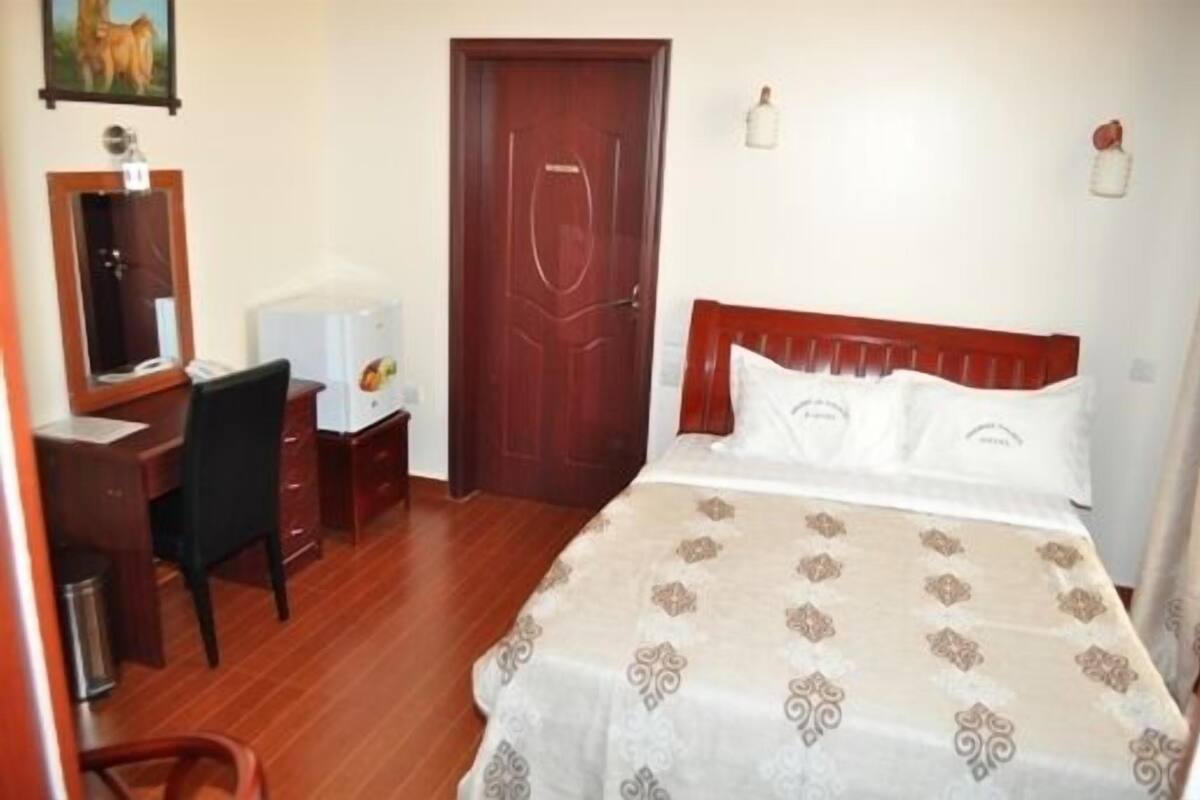 Quarto com cama de madeira, uma escrivaninha com cadeira, guarda-roupa e uma porta.