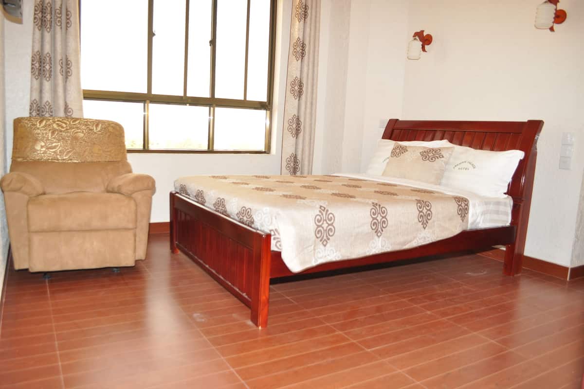 Quarto com cama de madeira, uma poltrona bege e uma janela com cortinas.