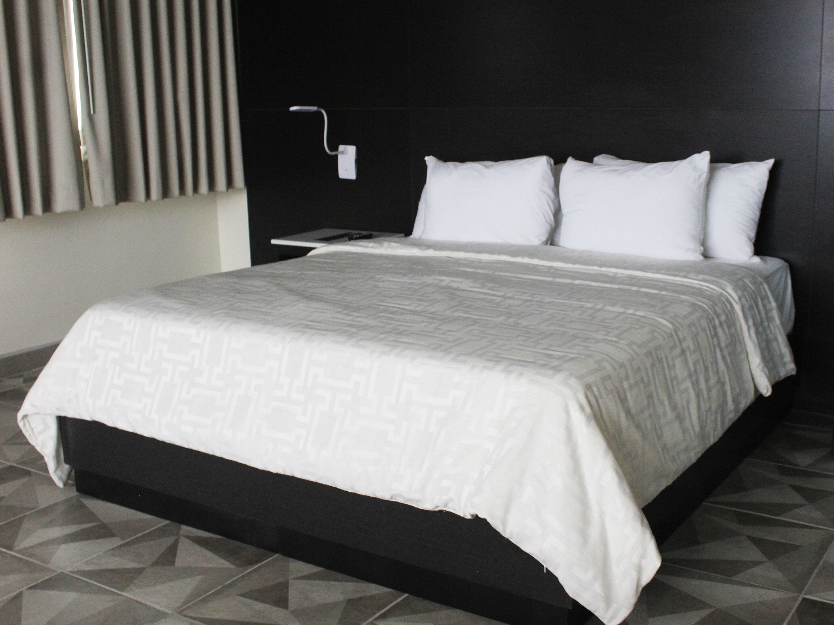 Quarto moderno com uma cama grande, roupa de cama branca, cabeceira preta e mesa de cabeceira com abajur.