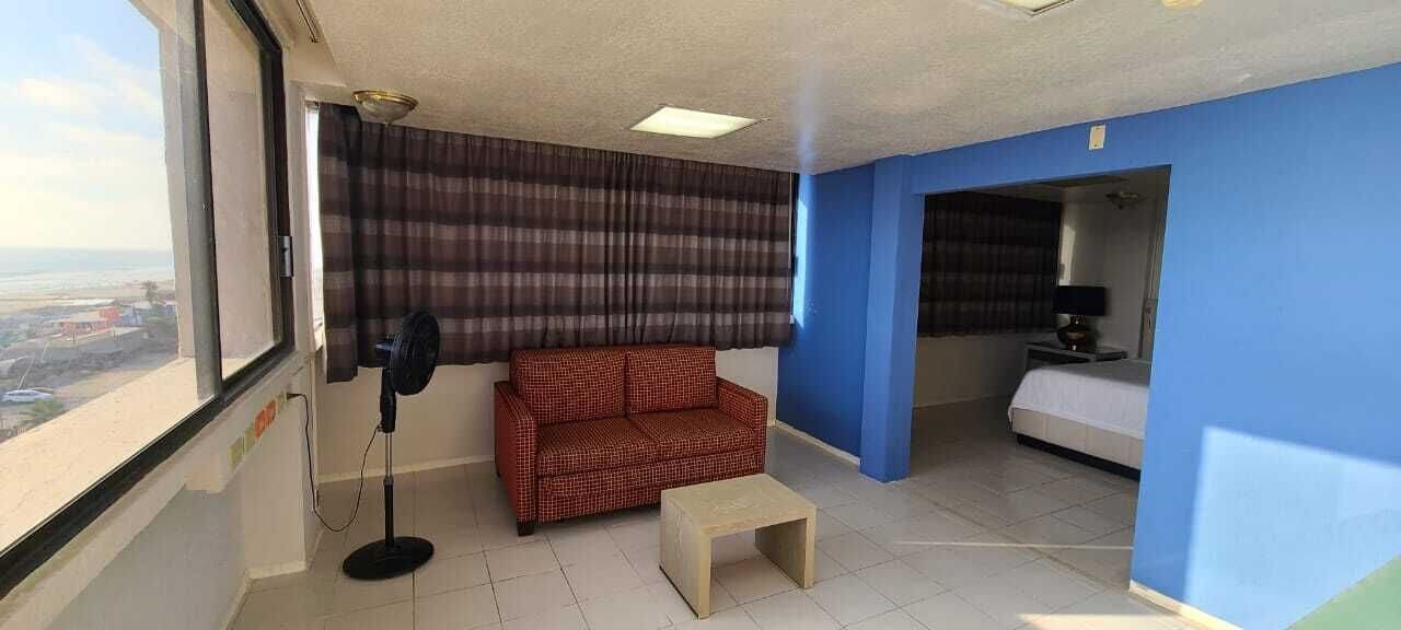 Um quarto com uma grande janela, um sofá de estampa xadrez vermelha, um banquinho de madeira e uma cama com parede azul.