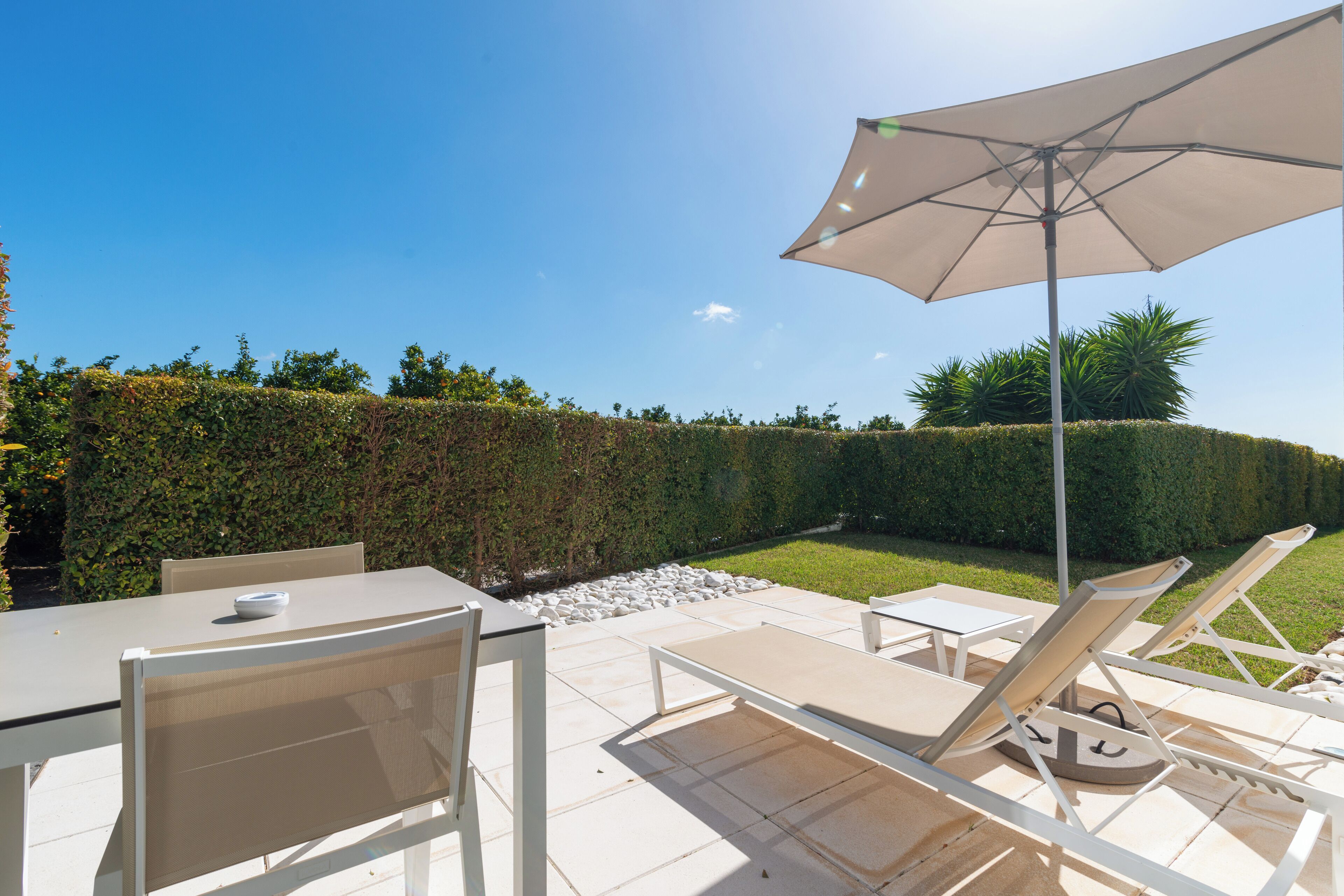 Um pátio externo com uma mesa, cadeiras e um guarda-sol.