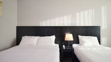Quarto de hotel com duas camas, uma mesa de cabeceira com abajur e uma parede lisa.