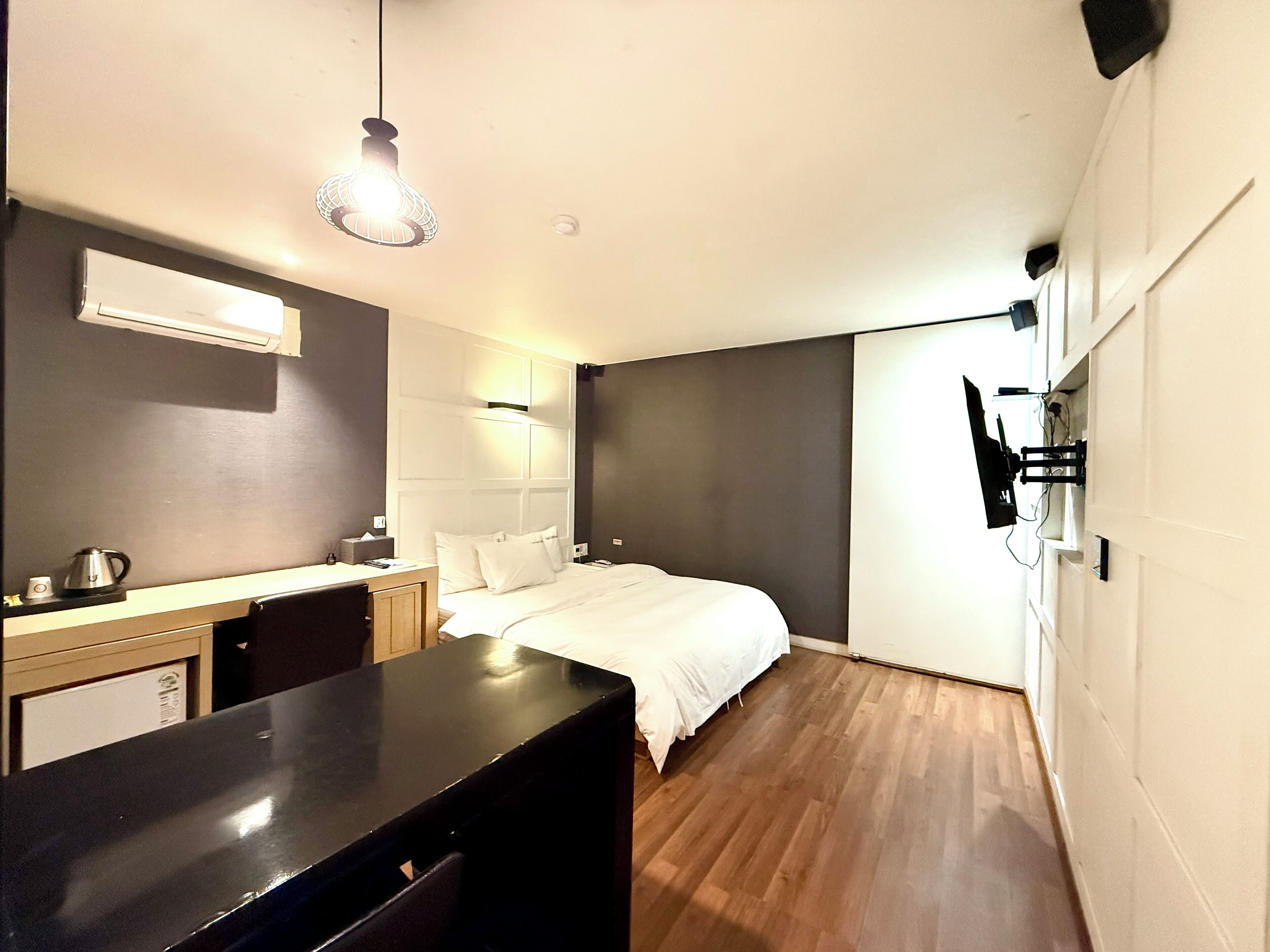 Quarto de hotel moderno com cama, escrivaninha, chaleira e televisão na parede.