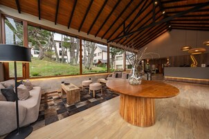 Um interior moderno com mesa de madeira central, área de estar e grandes janelas com vista para o exterior.