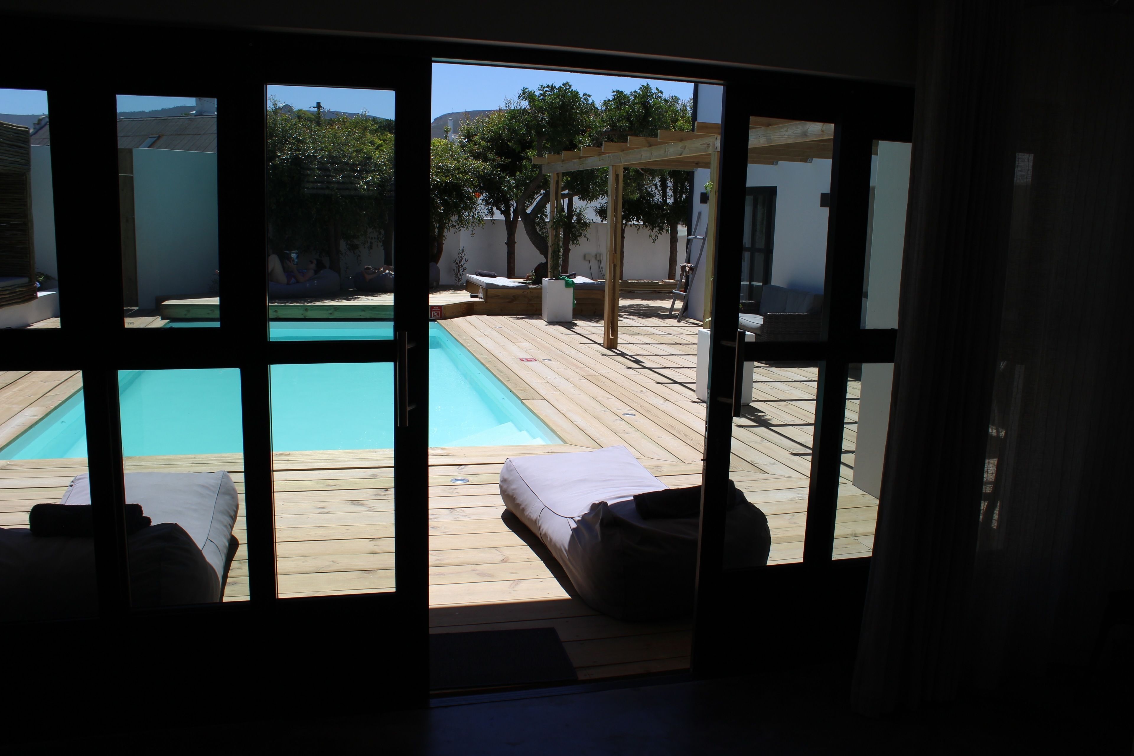 Vista de um deck de madeira com piscina, área de estar externa e uma pérgula.