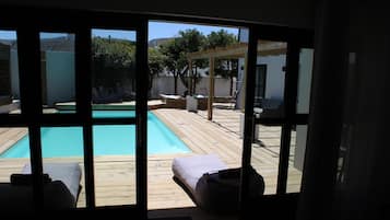Vista de um deck de madeira com piscina, área de estar externa e uma pérgula.