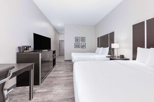 Quarto de hotel com cama, escrivaninha, televisão e guarda-roupa.