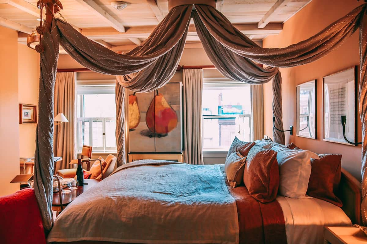 Quarto com cama de dossel, escrivaninha com cadeira e grande janela com cortinas.