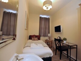 Quarto de hotel com cama, mesa de cabeceira, cadeira, escrivaninha, televisão e cortinas.