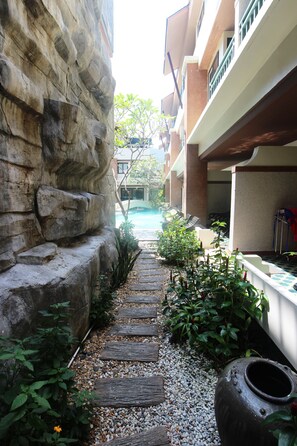 Um caminho de pedras leva a uma área de piscina com deck de madeira e vegetação.
