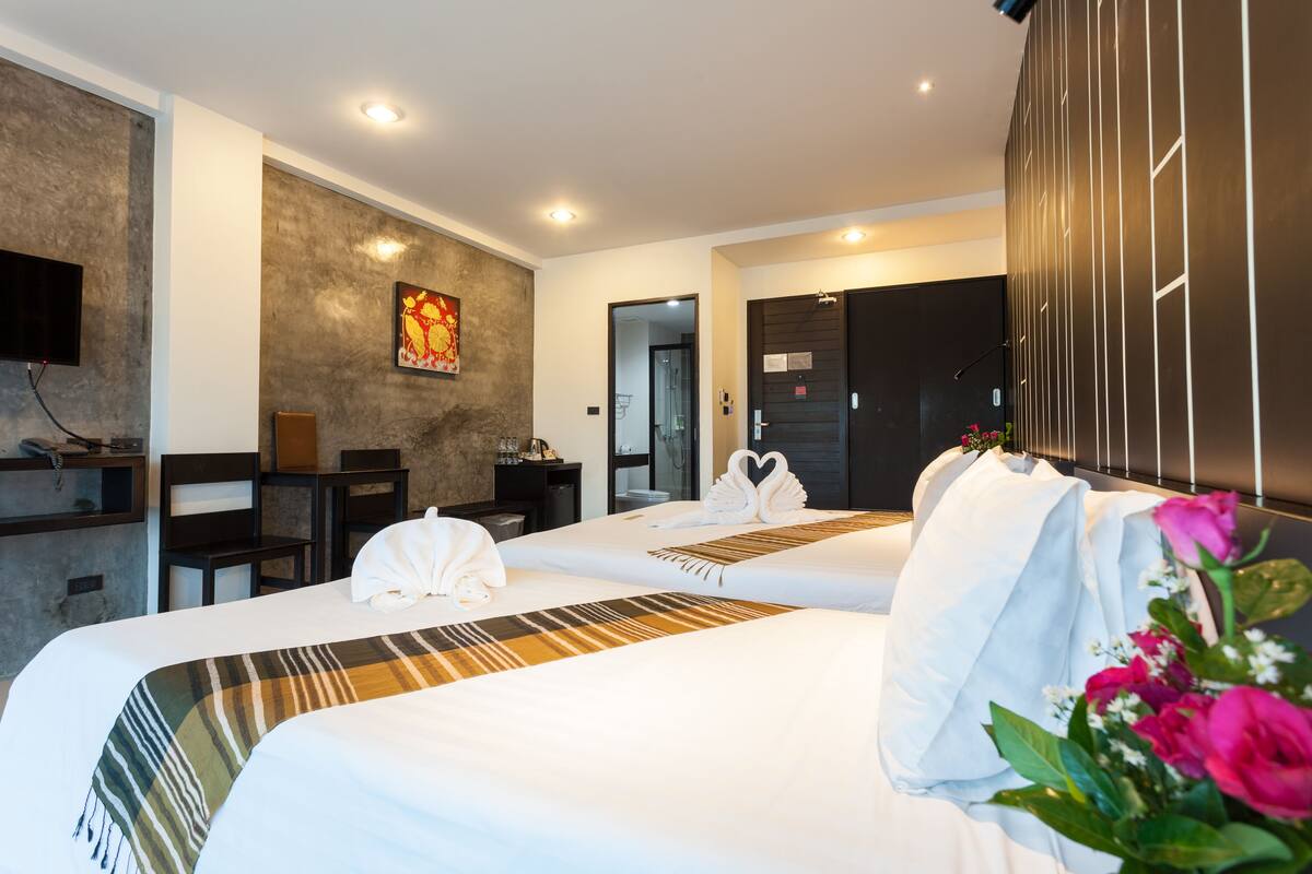 Quarto de hotel com duas camas, uma escrivaninha, uma televisão e uma porta.