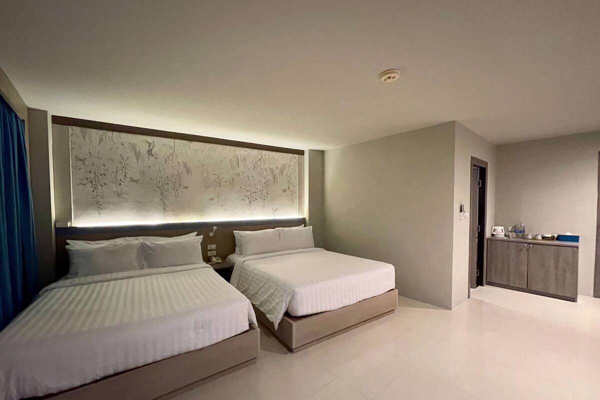 Quarto de hotel moderno com duas camas, uma obra de arte grande fixada na parede, uma pequena escrivaninha e uma área de cozinha compacta.