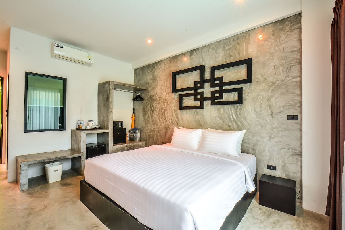 Quarto de hotel moderno com uma cama grande, um banco, uma pequena escrivaninha e ar-condicionado fixado na parede.