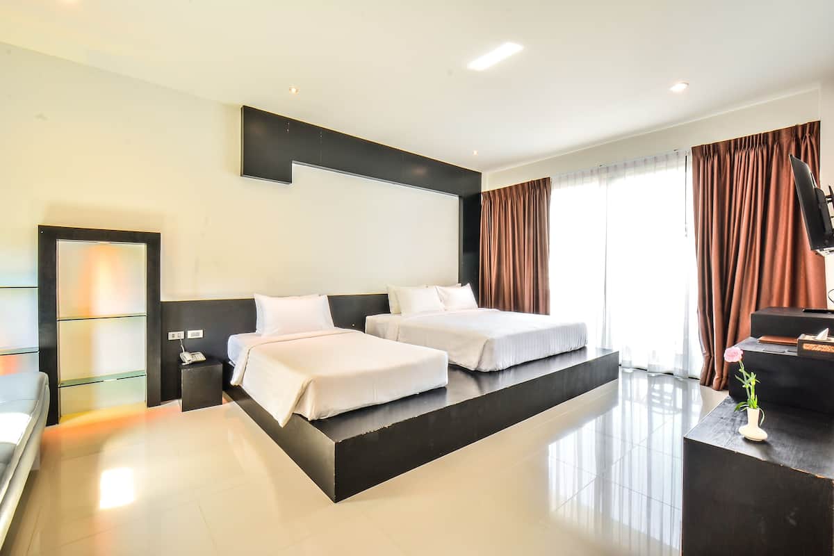 Quarto de hotel moderno com duas camas, televisão de tela plana, escrivaninha com computador e uma janela grande com cortinas.