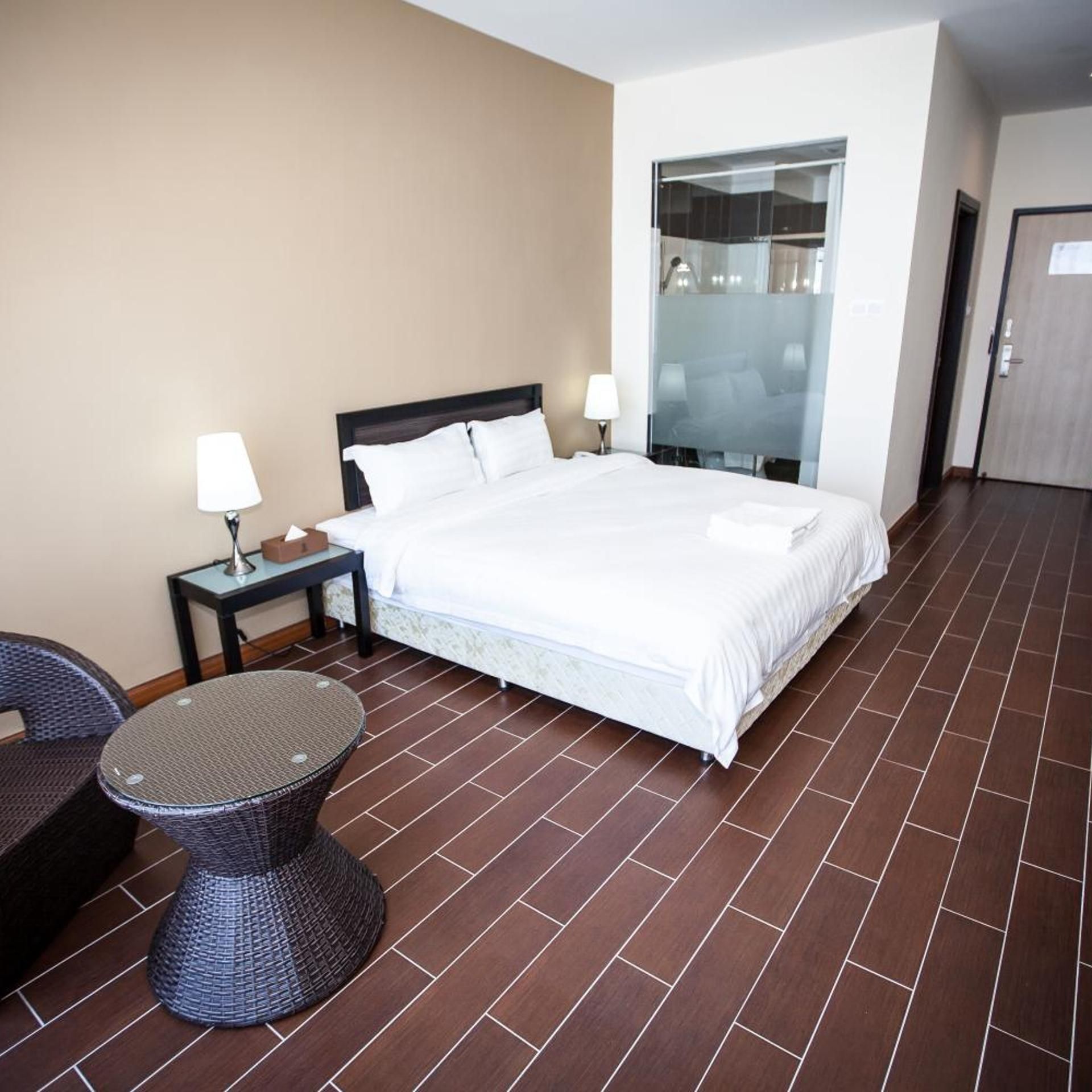 Quarto de hotel com uma cama grande, duas mesas de cabeceira com luminárias, uma mesa redonda e um painel de parede de vidro.