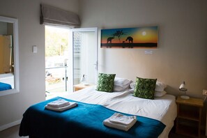 Quarto de hotel com cama, mesa de cabeceira, janela e um quadro de elefantes na parede.