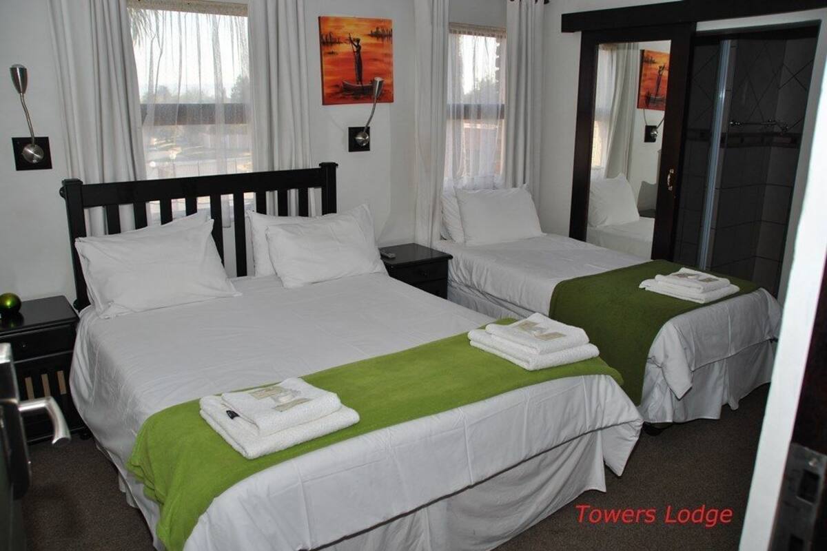 Quarto de hotel com duas camas, roupa de cama branca, colchas verdes e uma toalha verde em cada cama.
