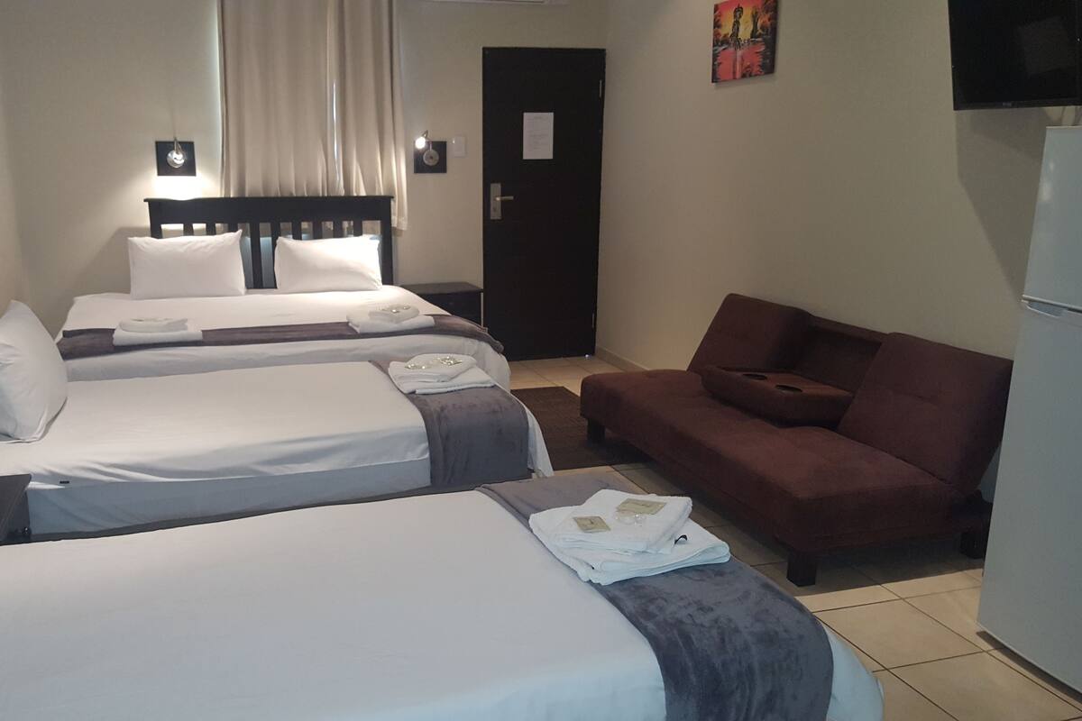 Quarto de hotel com duas camas de solteiro, um sofá, uma televisão e uma porta com um aviso.