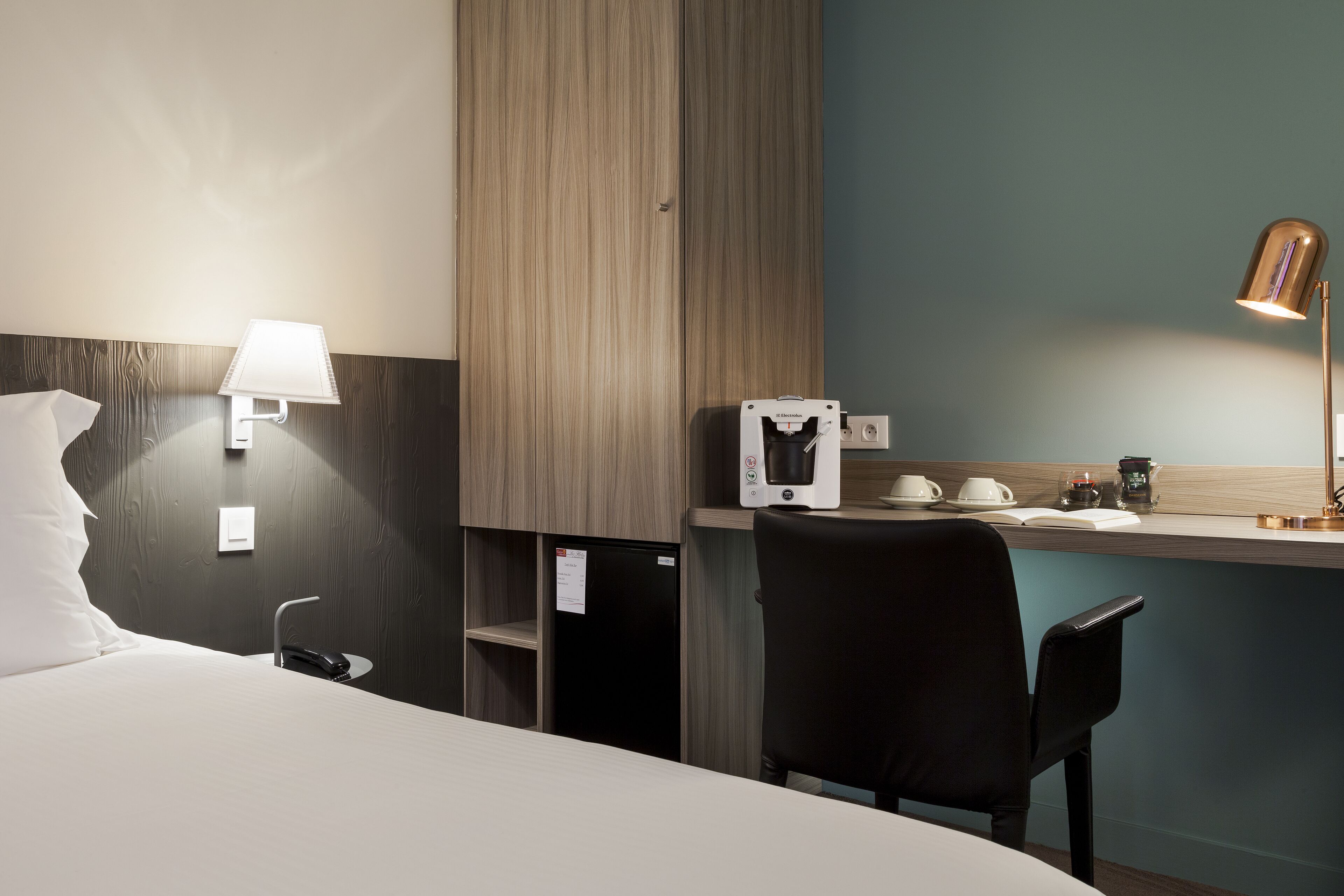 Quarto de hotel com cama, escrivaninha, cafeteira, luminária e cadeira.