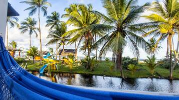 Uma rede com vista para uma piscina, palmeiras e um pequeno espelho d'água.